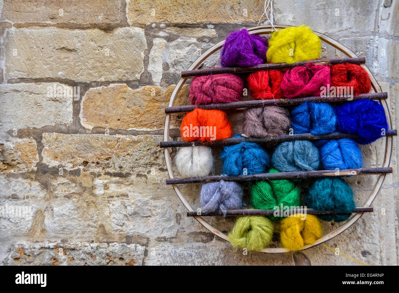 Balls of brightly coloured wool in a circular display on a brick wall ...