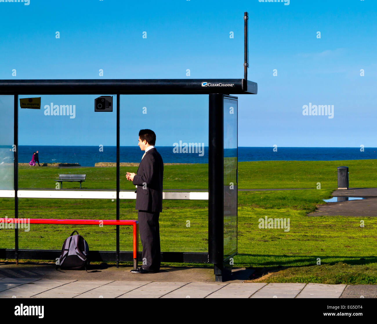 Young man in suit waiting at a bus stop with the sea behind at Whitley ...
