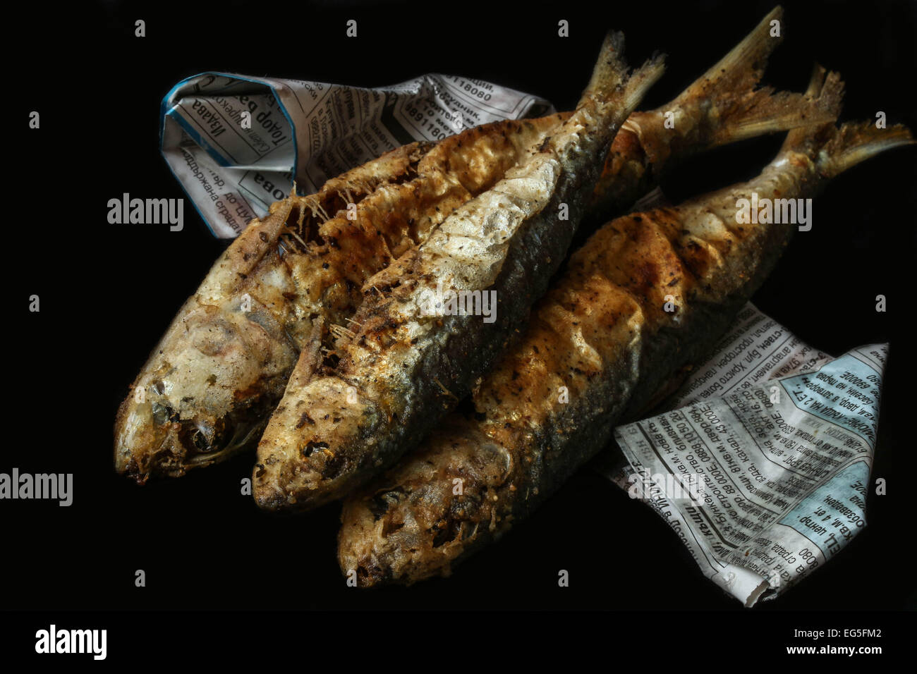 Fried fish on a newspaper - black background Stock Photo - Alamy