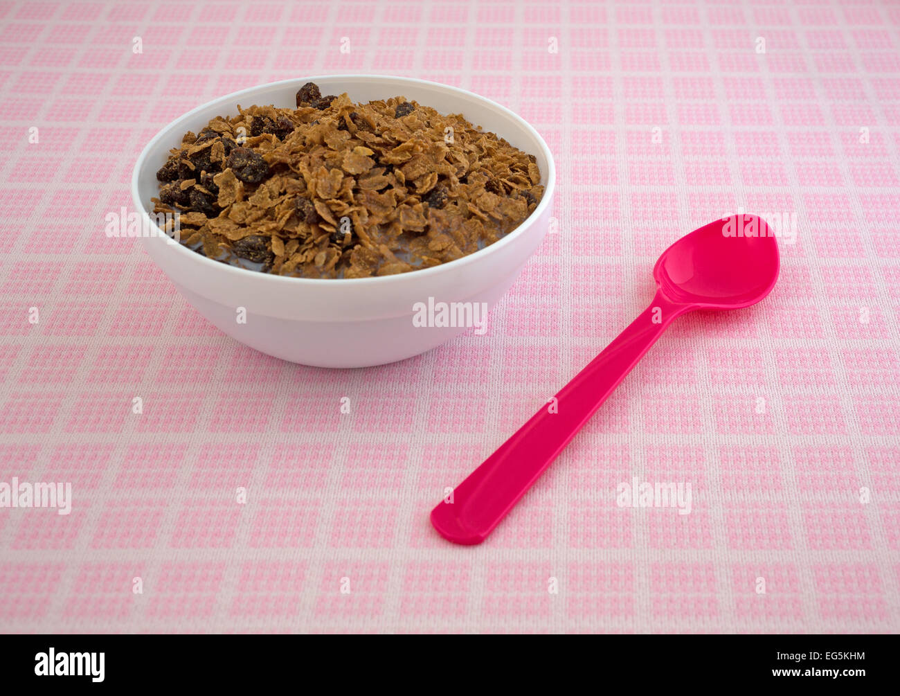 A bowl of whole grain raisin bran on a table cloth with a pink spoon to ...