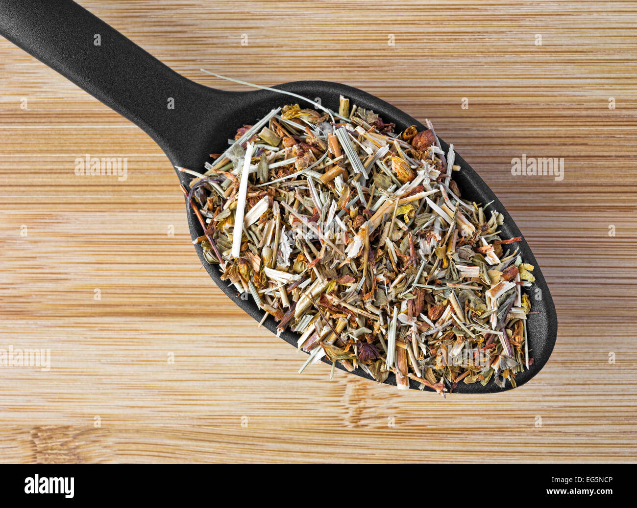 Shredded and dried St. Johns Wort in a black spoon atop a wood cutting ...