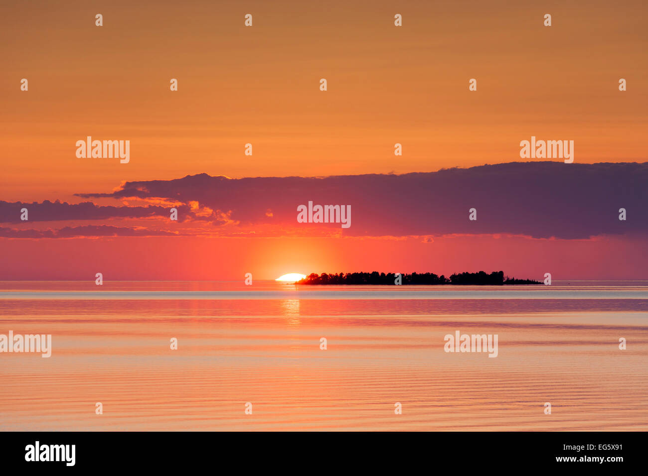 Sunset with sun setting behind silhouetted island in Lake Vänern ...