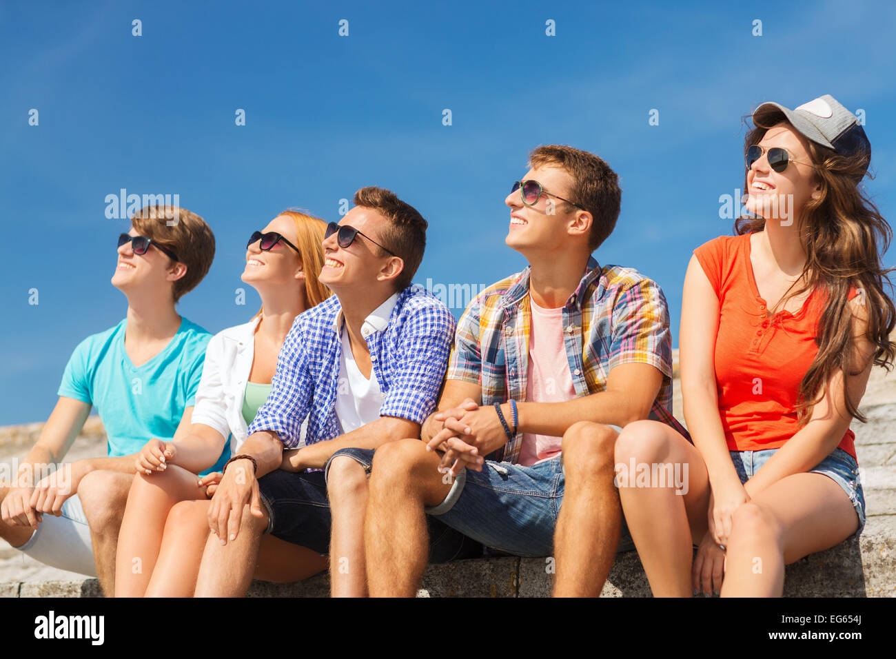 group of smiling friends sitting on city street Stock Photo - Alamy