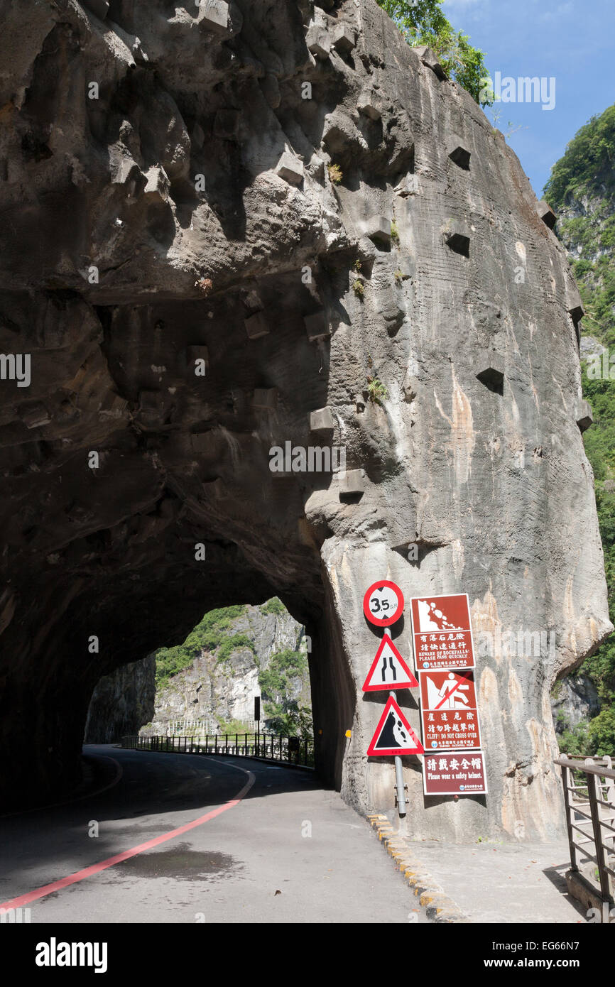 Caution signs next to the cliffside cemented tunnel and road along ...