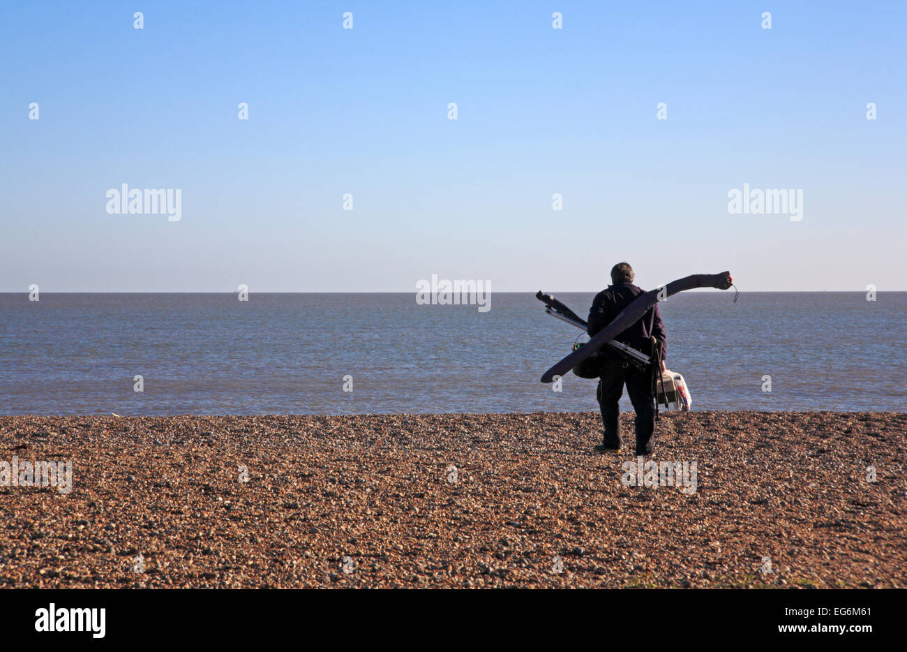 A sea angler with equipment walking across the shingle beach at Dunwich ...