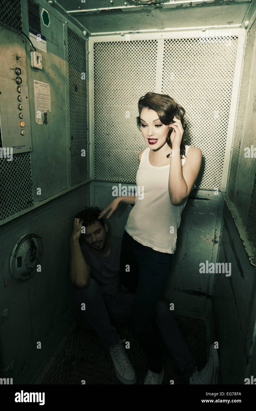 Attractive young woman in an old elevator with man sitting on ground ...