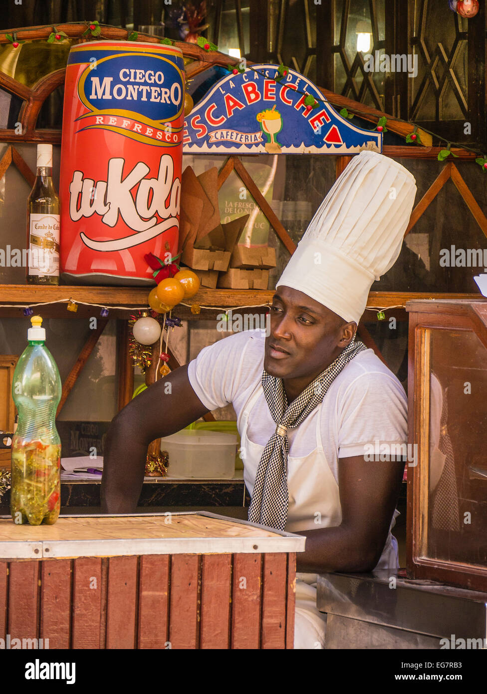 An Afro-Cuban restaurant worker in a tall white chef's hat takes a ...