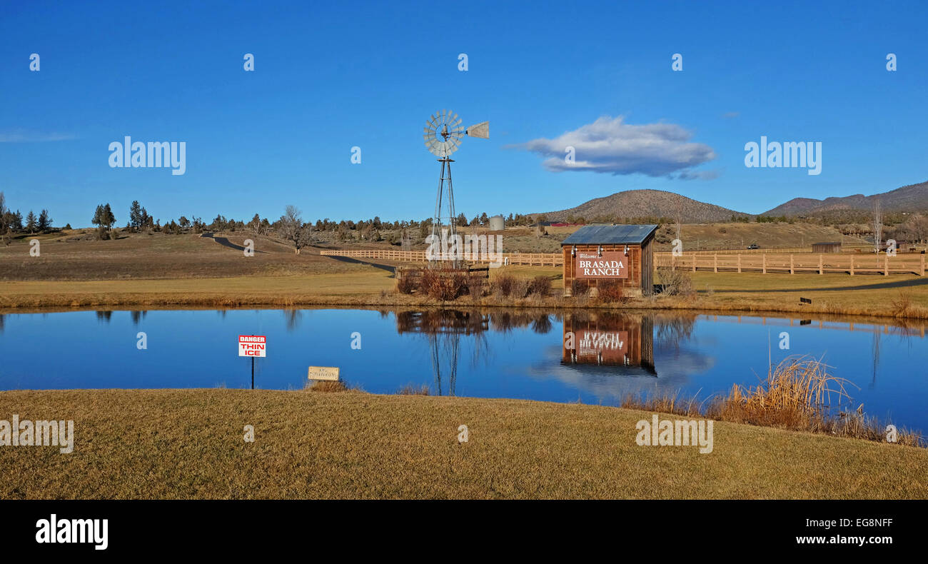 A ranch windmill is reflected in a ranch pond during a winter day at ...
