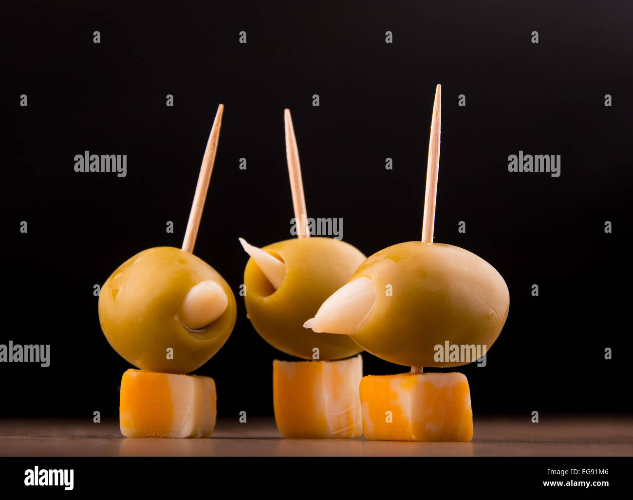 Green garlic stuffed olives and cheese cubes on toothpicks against dark ...