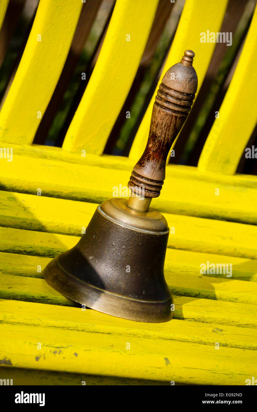 Traditional school hand bell on a yellow wooden bench during playtime ...