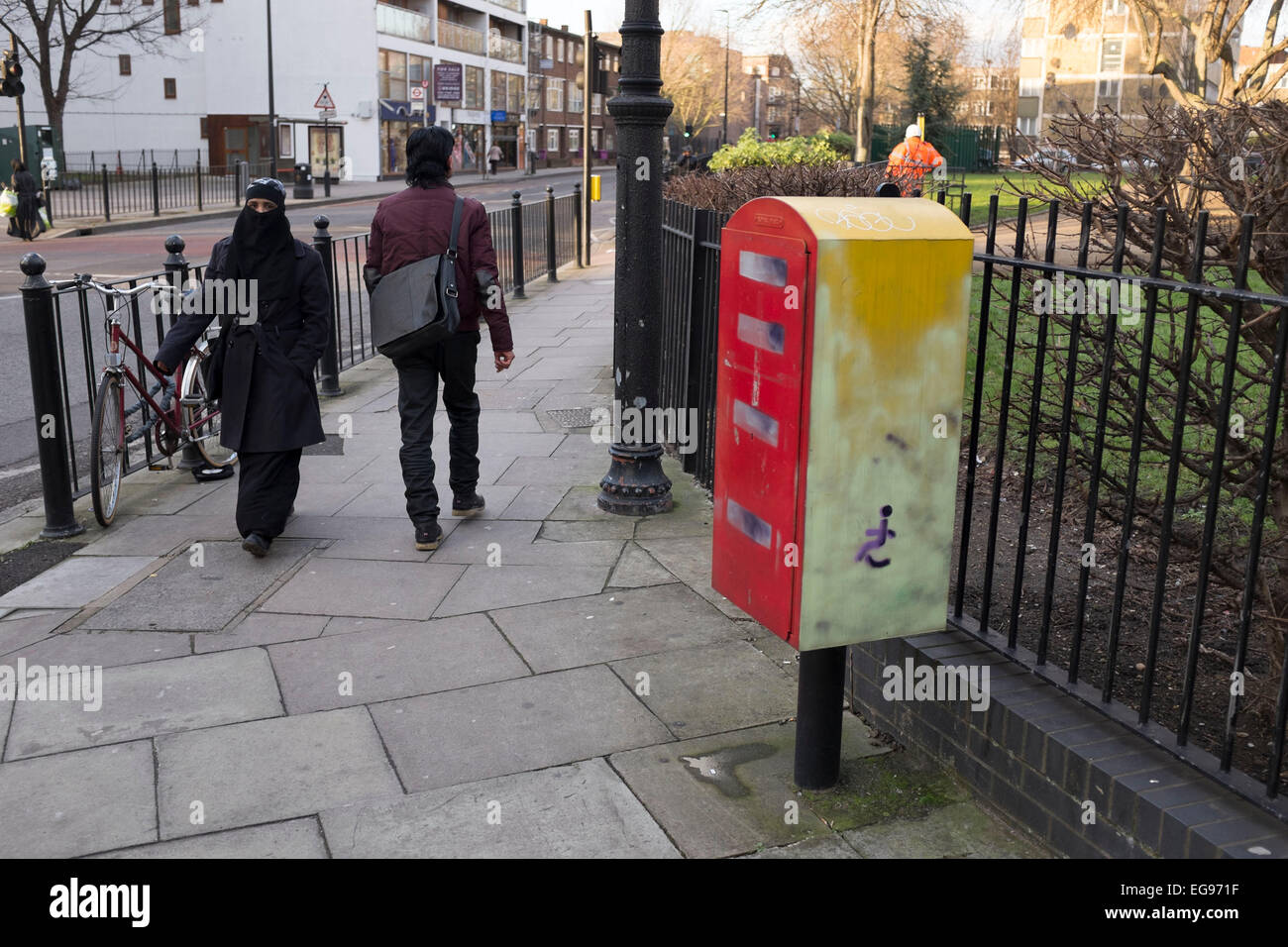 Muslim woman wearing a hijab walks past a Royal Mail post box on a ...