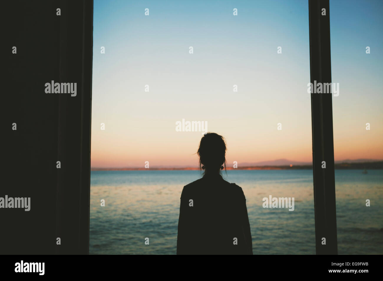 Woman looking at sea through window Stock Photo - Alamy