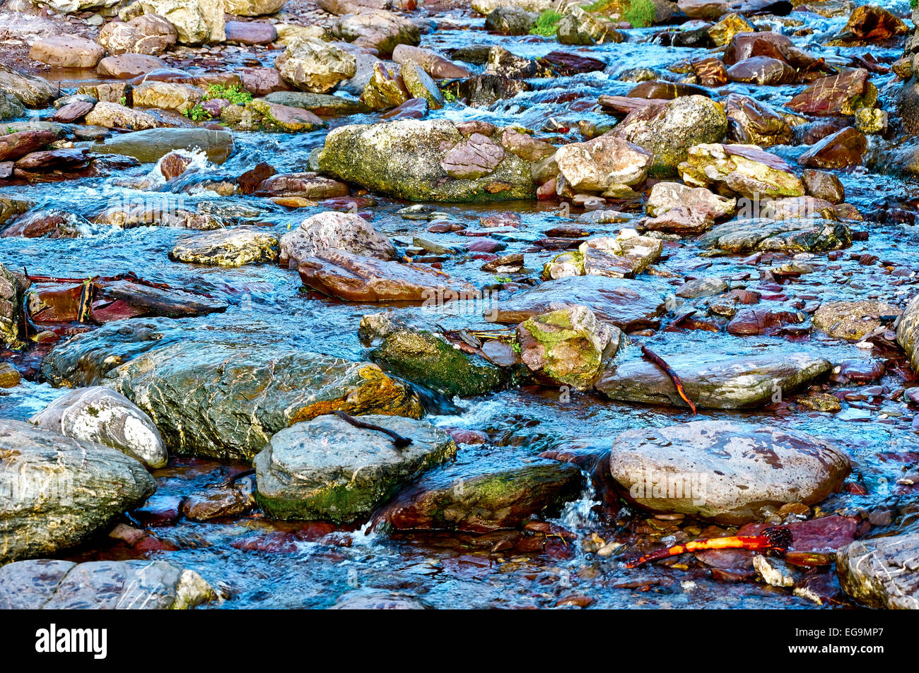 Blue sky reflected in sea water as it washes over rocks and stones on ...
