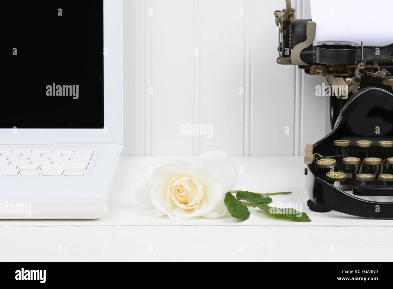 Closeup of a white desk with a rose laying between a modern laptop ...
