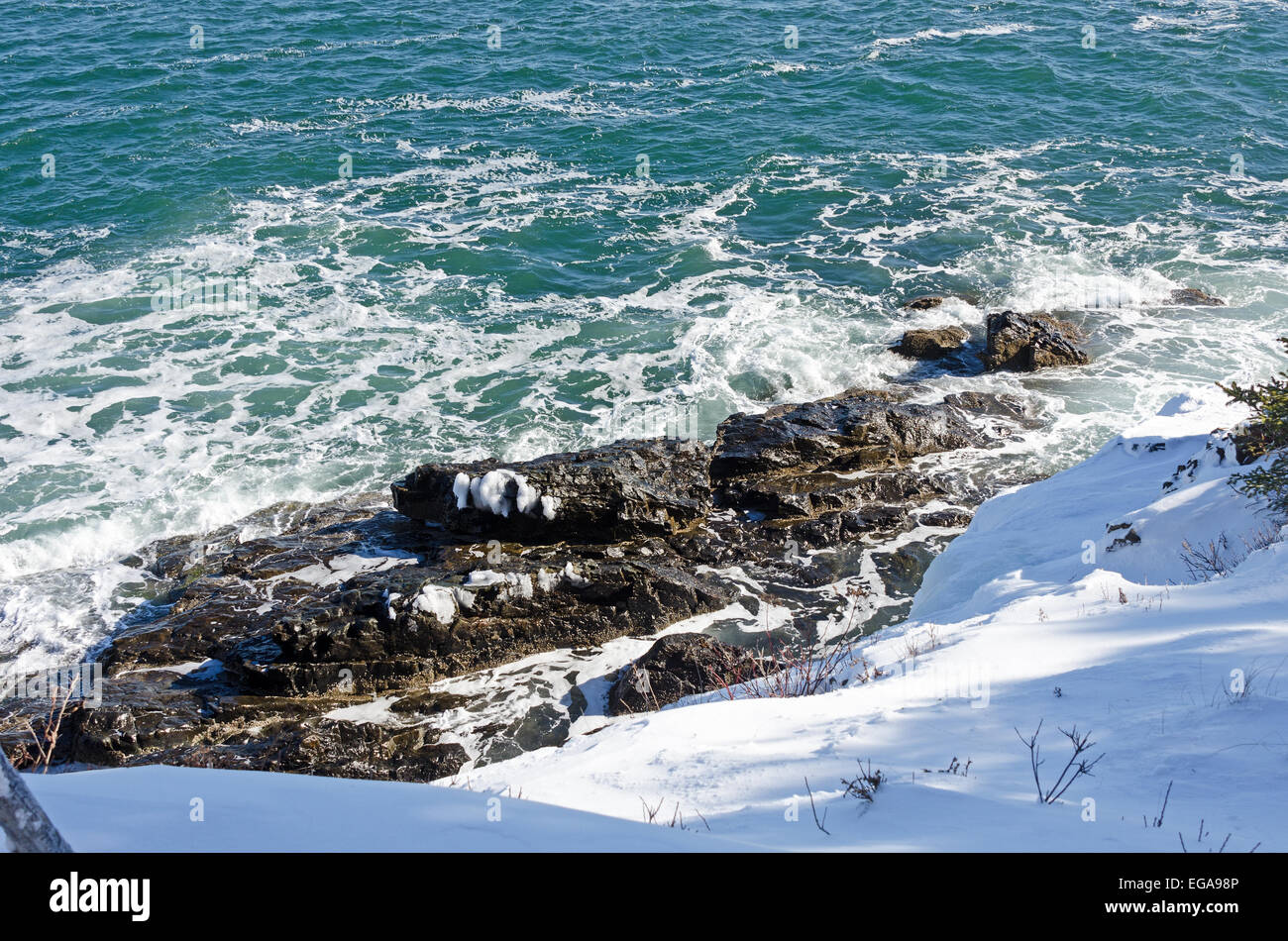 Waves breaking on ice-covered rocks at the foot of a cliff in Acadia ...