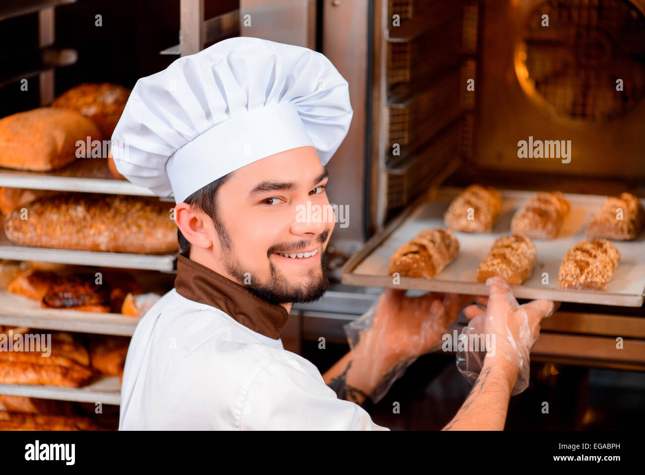Fresh baked bread. Confident young man in apron taking the fresh baked ...