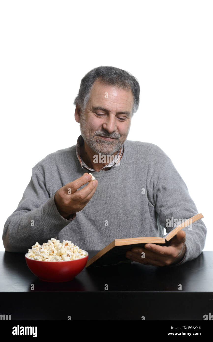Middle aged man reading a book while eating popcorn at home Stock Photo ...