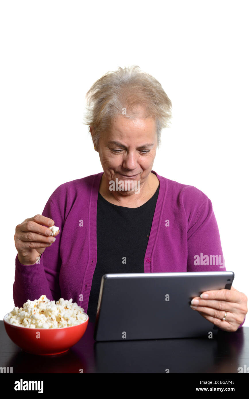 Middle aged woman using a tablet computer while eating popcorn at home ...
