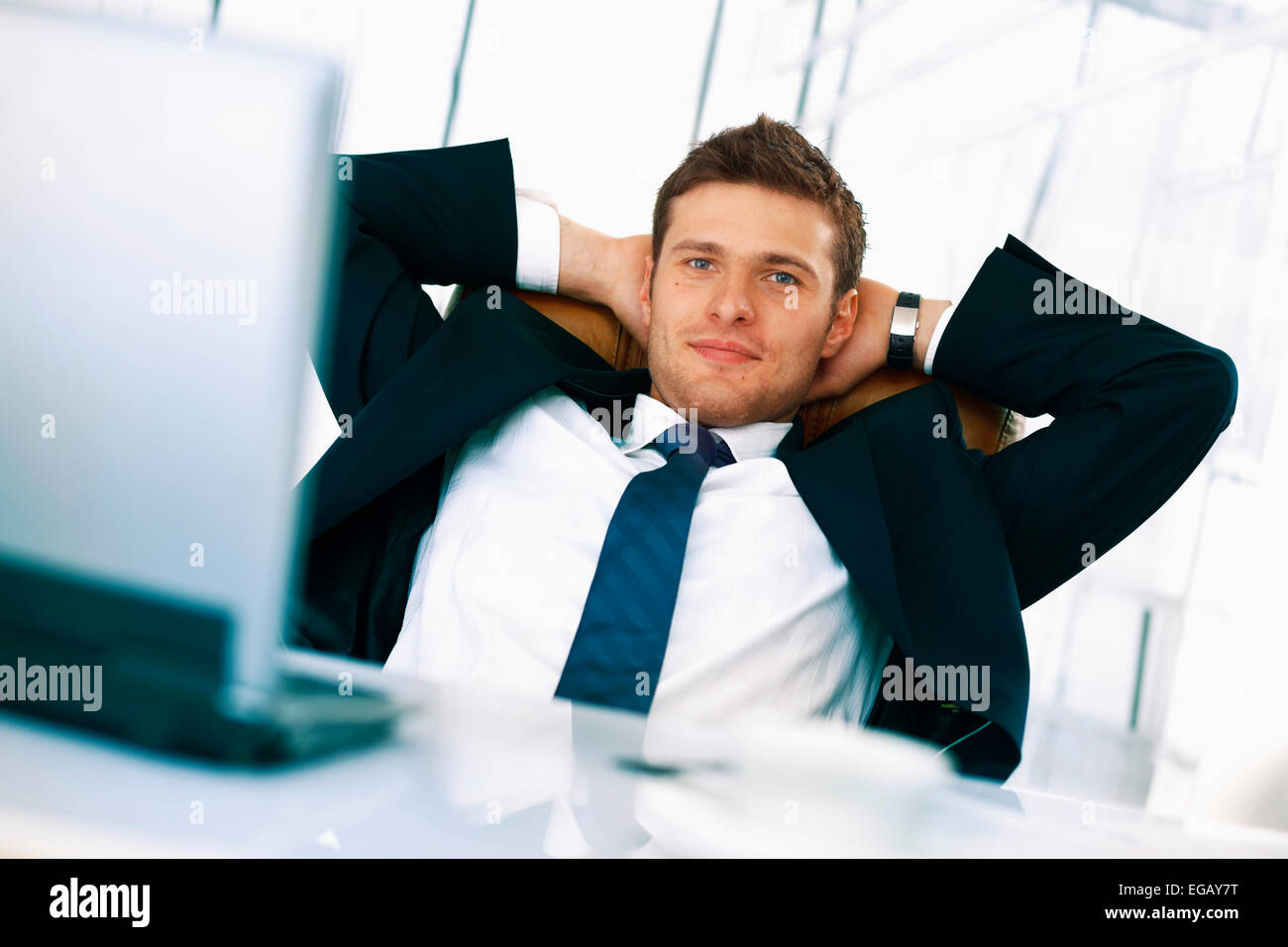 Young businessman sitting relaxed in his chair with hands under his ...
