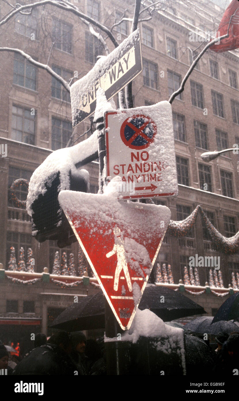 A traffic light pole with traffic signs is covered with snow on ...