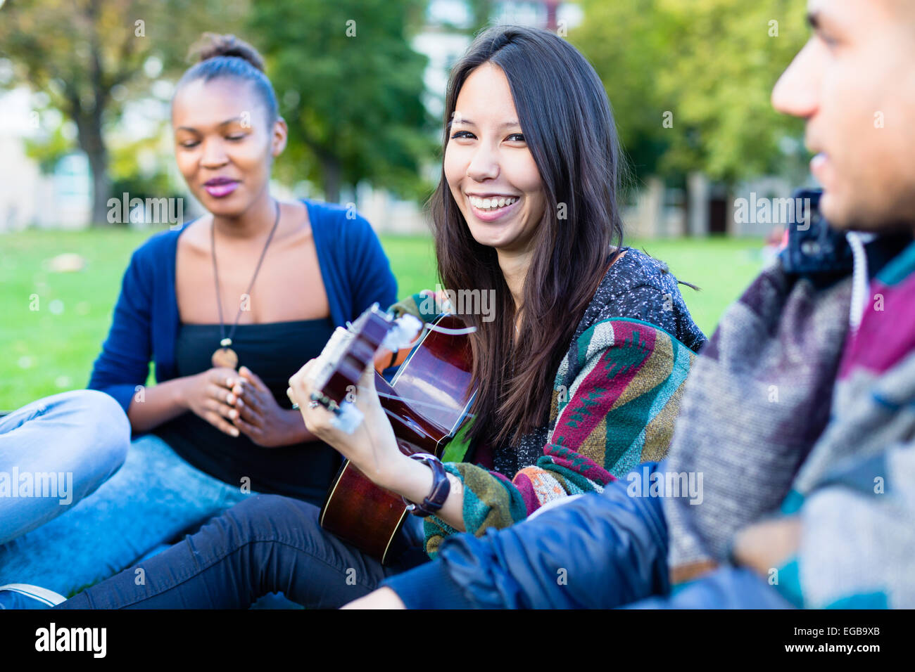 Friends singing songs in park having fun together with one girl playing ...