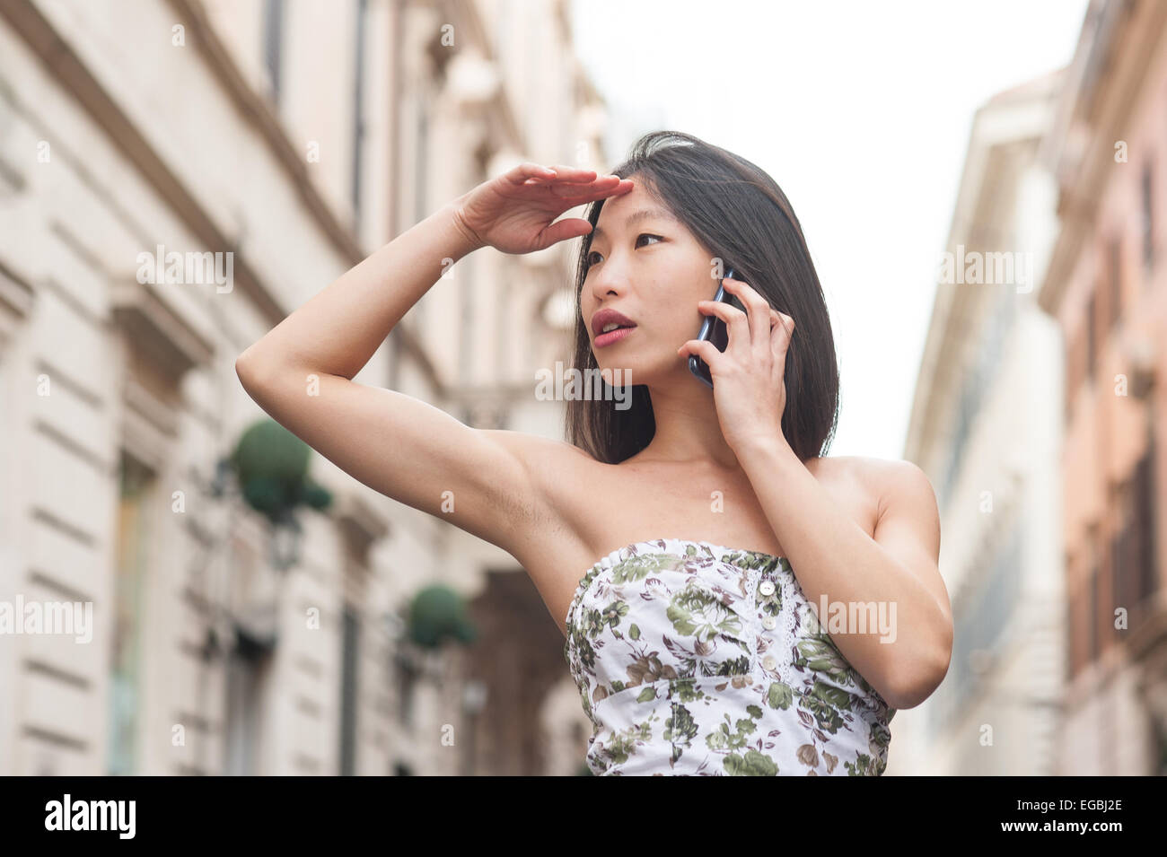 Young beautiful asian woman looking around and talking using mobile ...