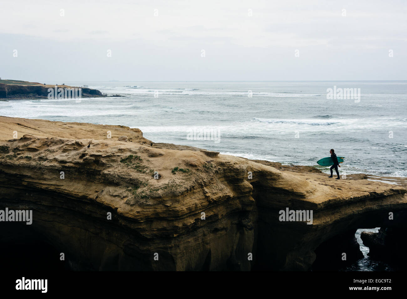 Surfer walking on cliffs along the Pacific Ocean at Sunset Cliffs ...