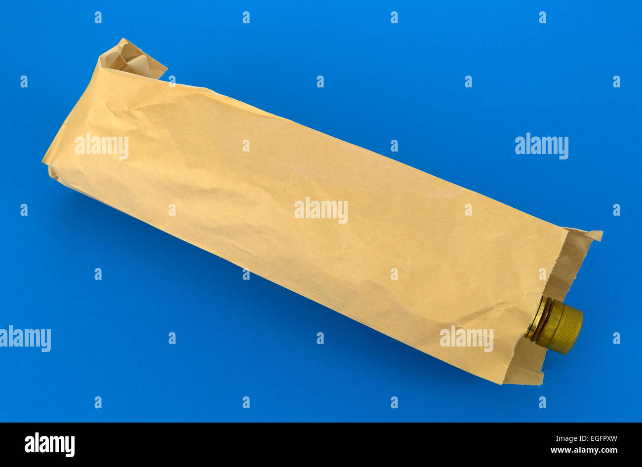 A bottle of whiskey in a plain brown paper bag laying on a blue ...
