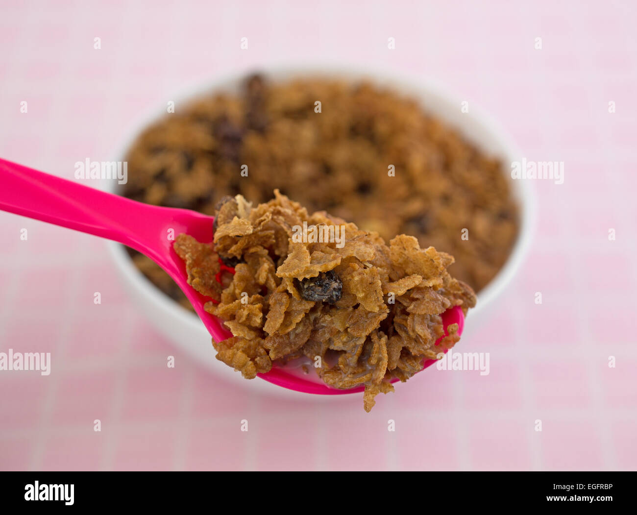 Close view of a pink spoon full of whole grain raisin bran with a white ...