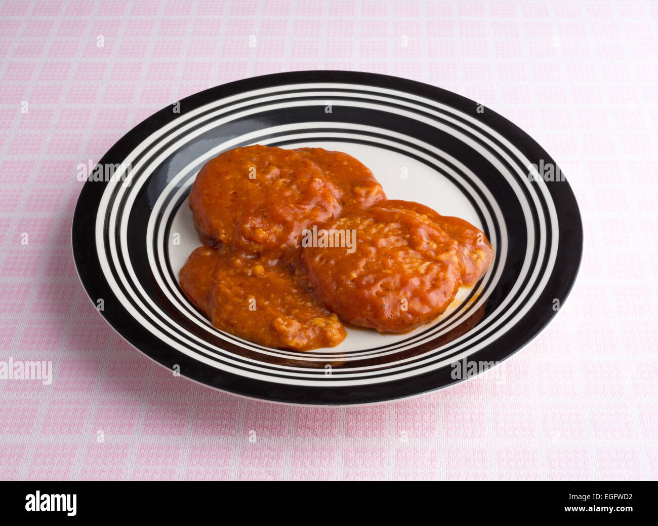 A serving of prepared chicken parmigiana on a plate upon a pink ...