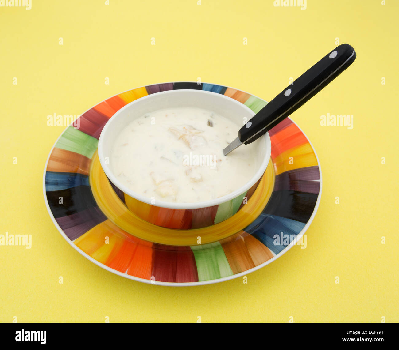 A bowl of clam chowder with potatoes in a colorful bowl atop a plate ...