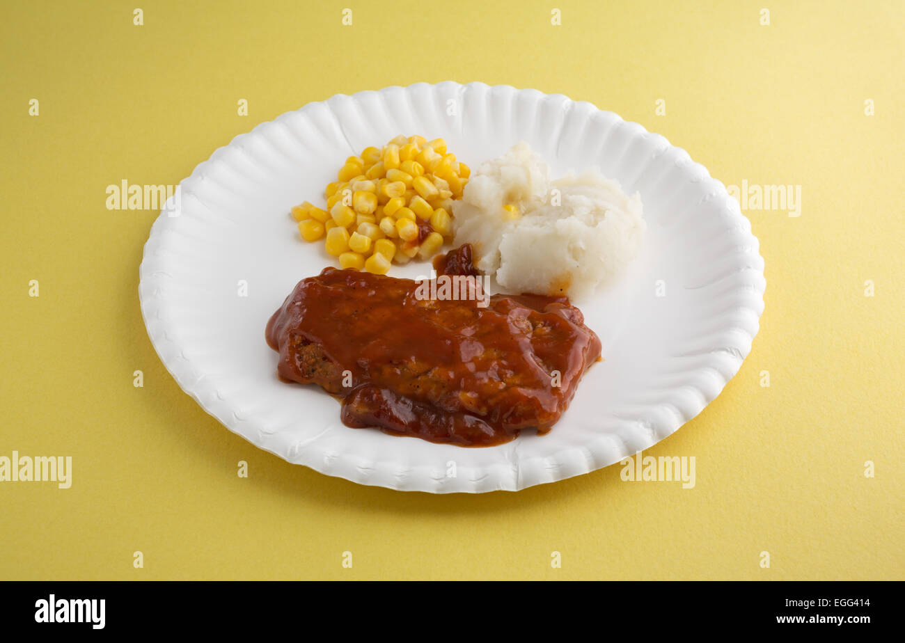 A plain pork in gravy TV dinner on a paper plate with corn and mashed ...