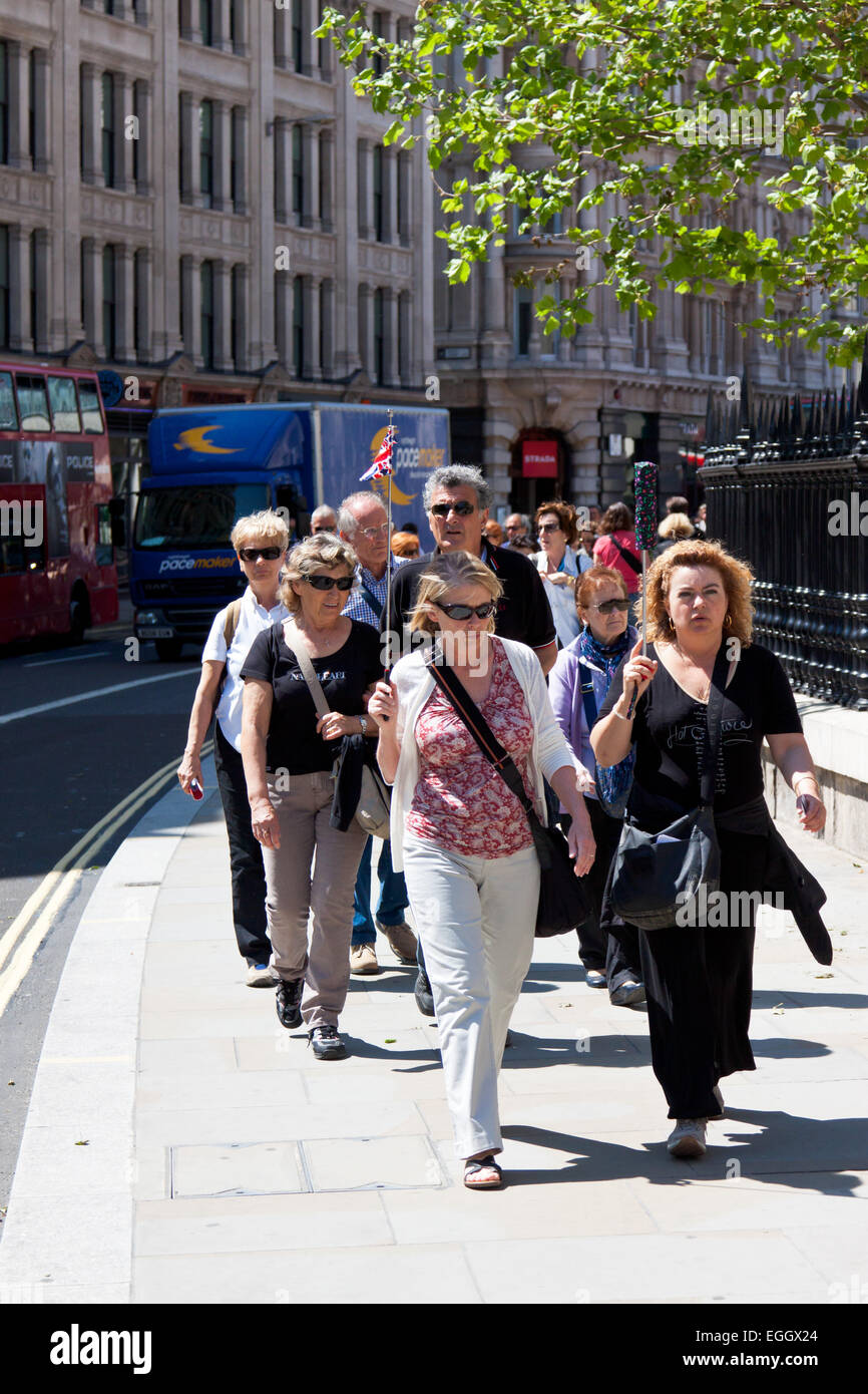 Tour group walking through London with tour leaders holding up a flag ...