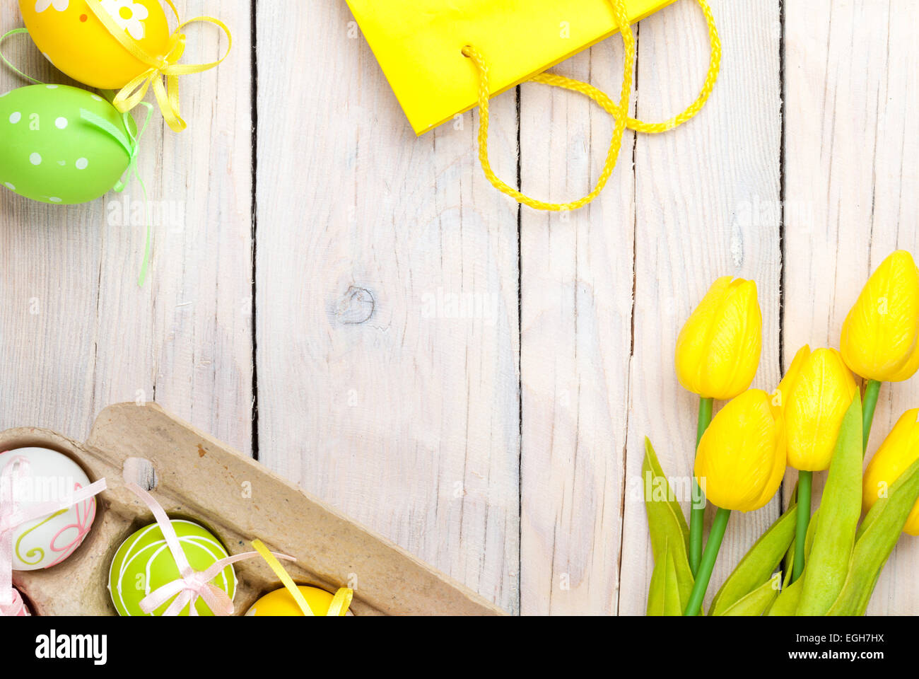 Easter background with colorful eggs and yellow tulips over white wood ...