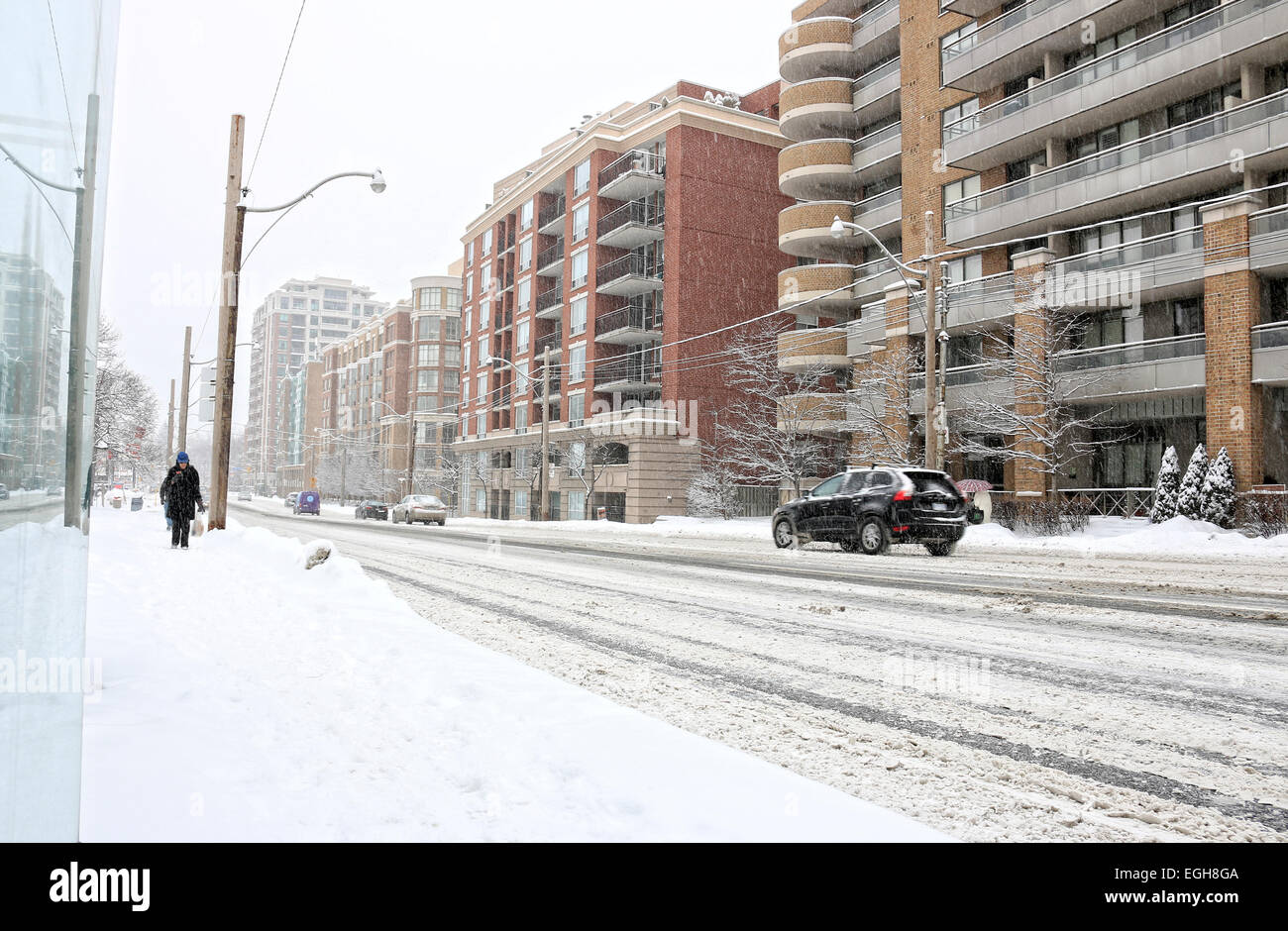 Snow falling on unplowed urban road with people walking and cars ...