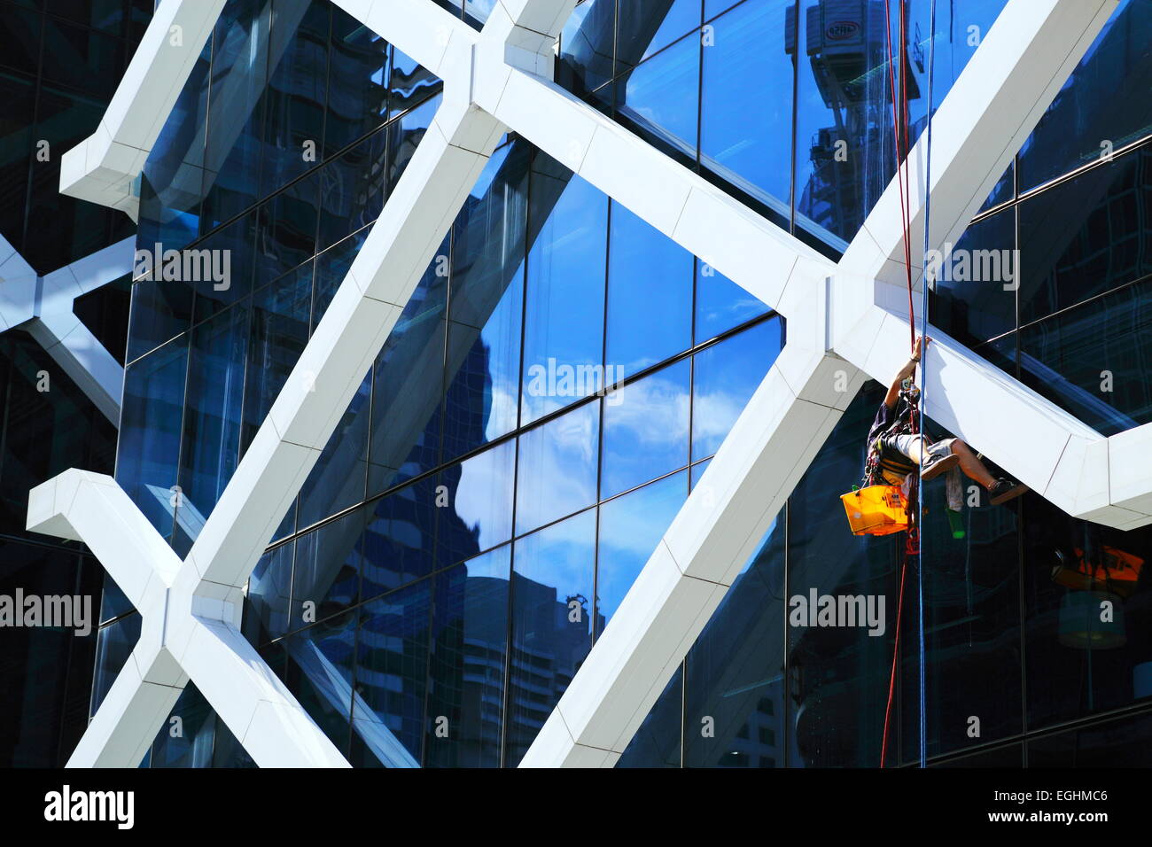 A window cleaner works suspended in a harness along with his tools of ...