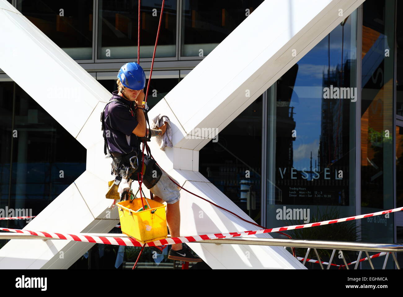 A window cleaner with blue helmet suspended in a harness along with his ...