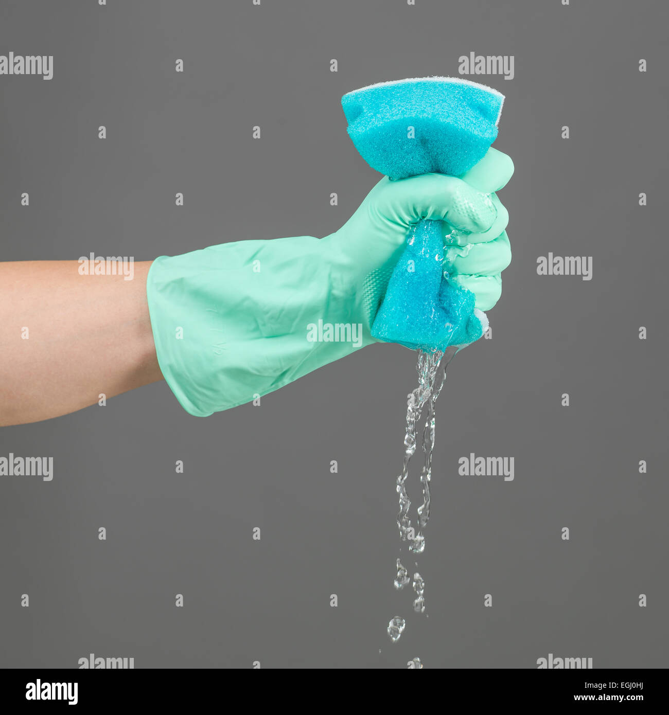 human hand with rubber glove squeezing water from sponge on grey ...