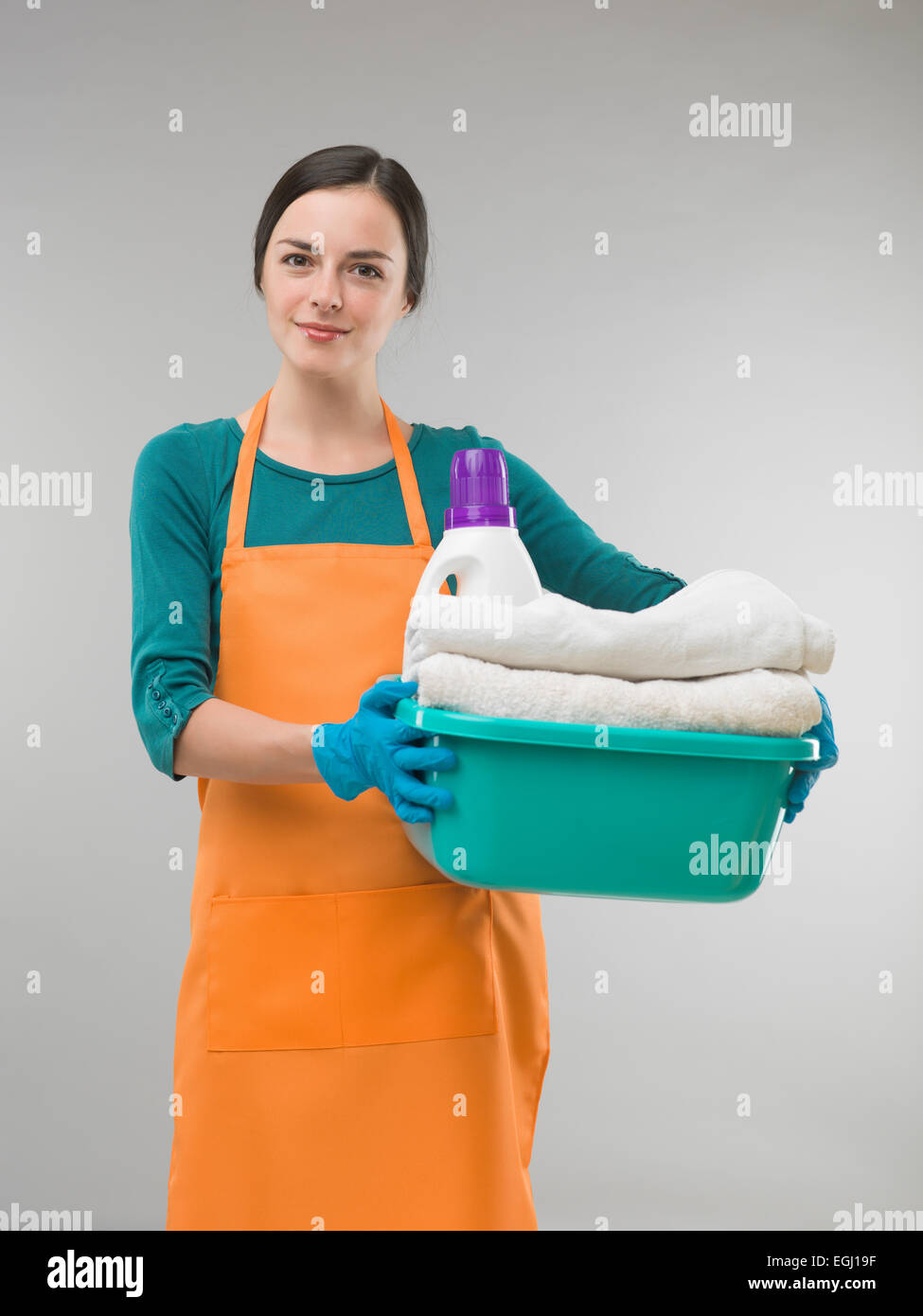 young woman holding clean towels and detergent in basin against grey background. studio ...