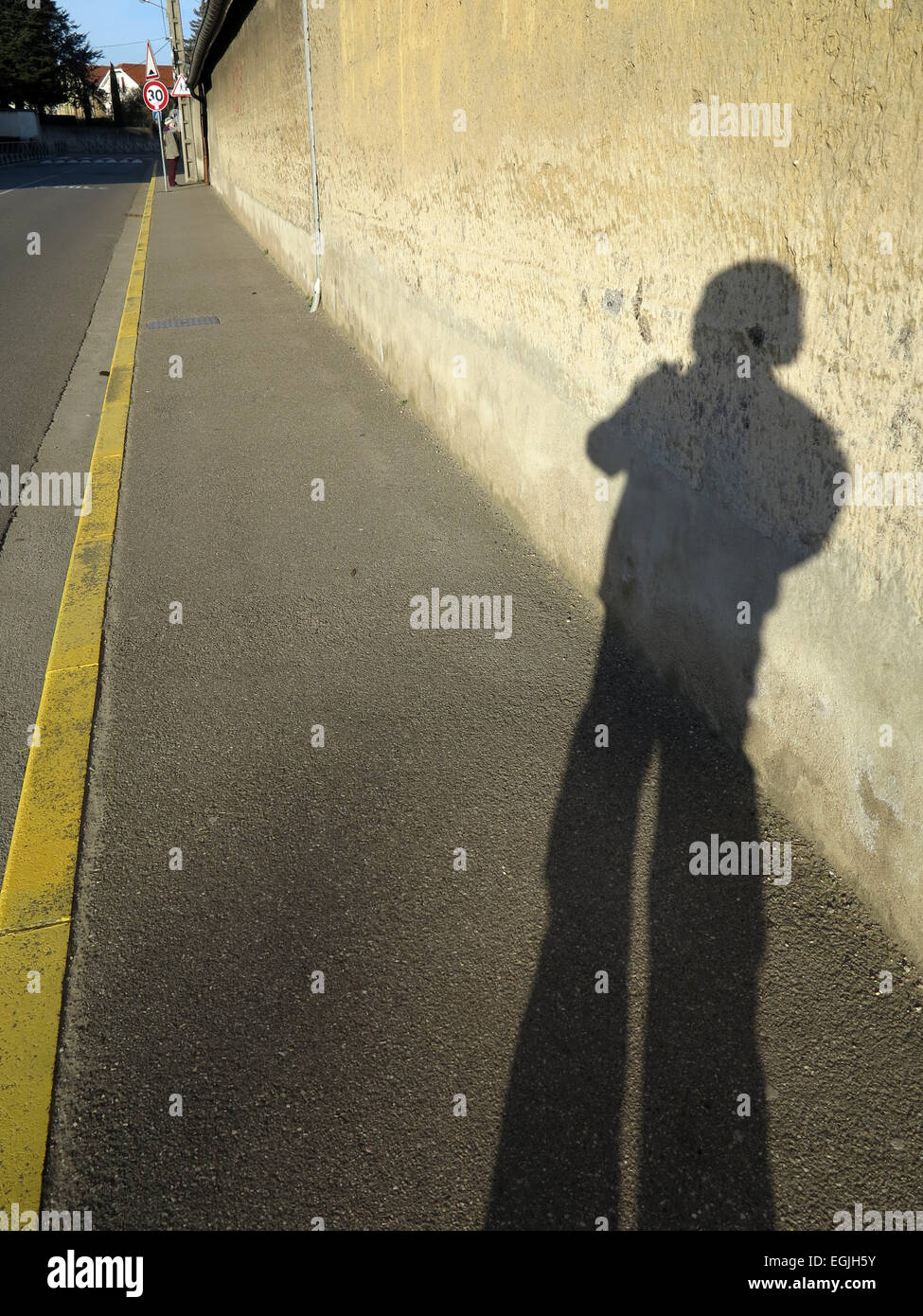 Long projected shadow of pedestrian on the footpath with pedestrian in ...