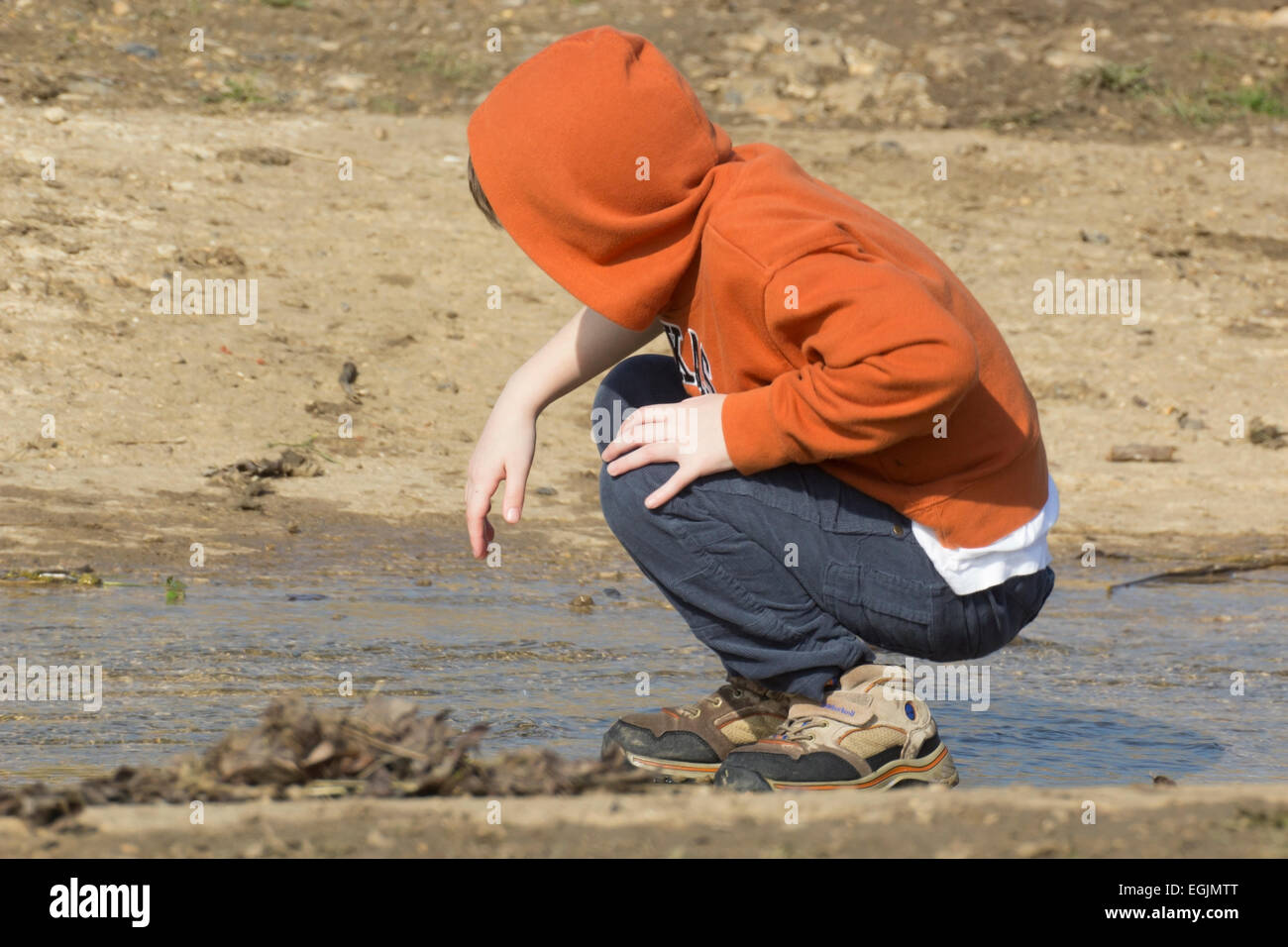 Boy crouching down feeling water next to river in Cambridgeshire ...