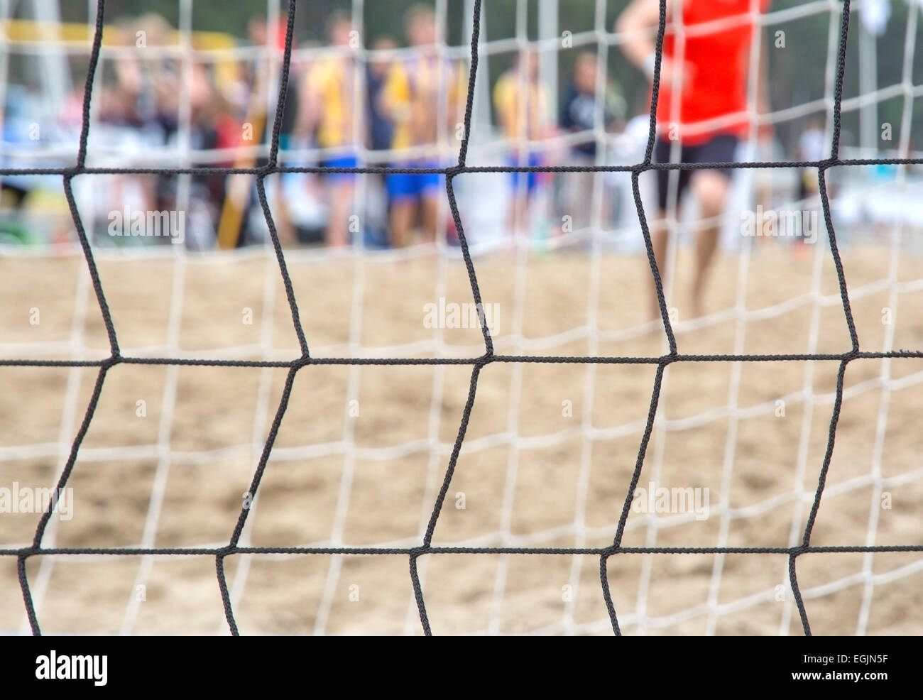 Beach soccer net closeup with people playing a game behind in blur ...
