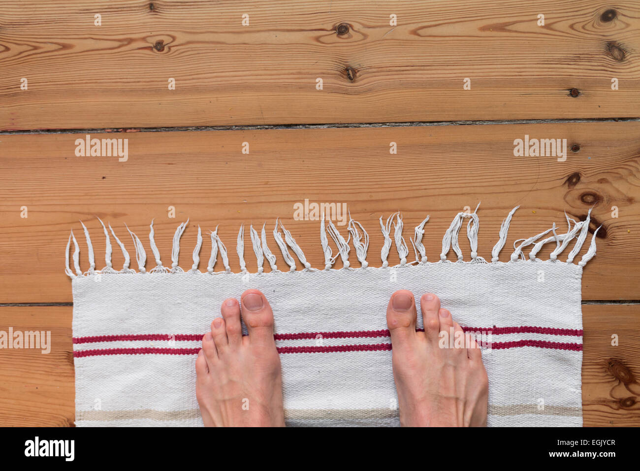 A man's feet on a white rug placed on a wooden floor. Overhead shot ...