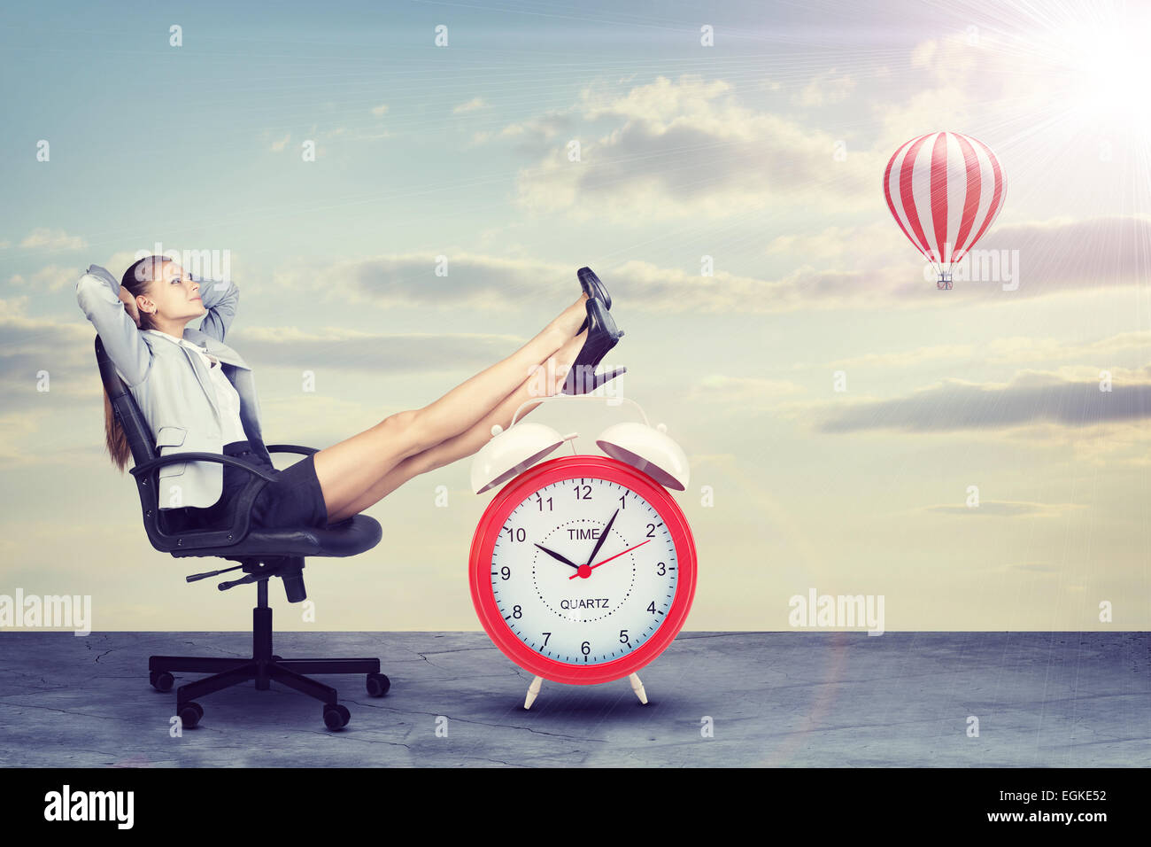 Businesswoman sitting with her feet up on alarm-clock Stock Photo - Alamy