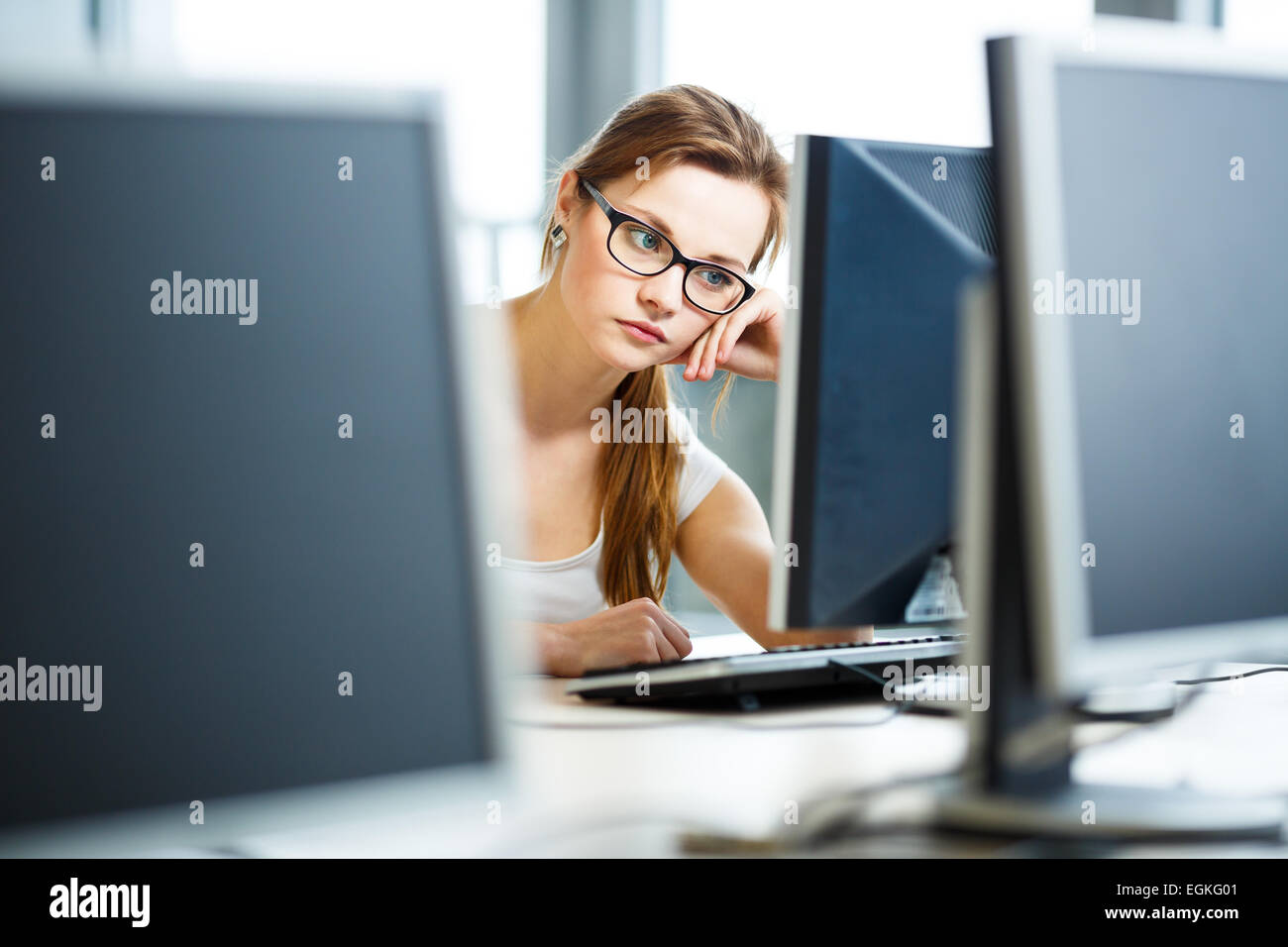 Pretty, female student looking at a desktop computer screen, learning ...