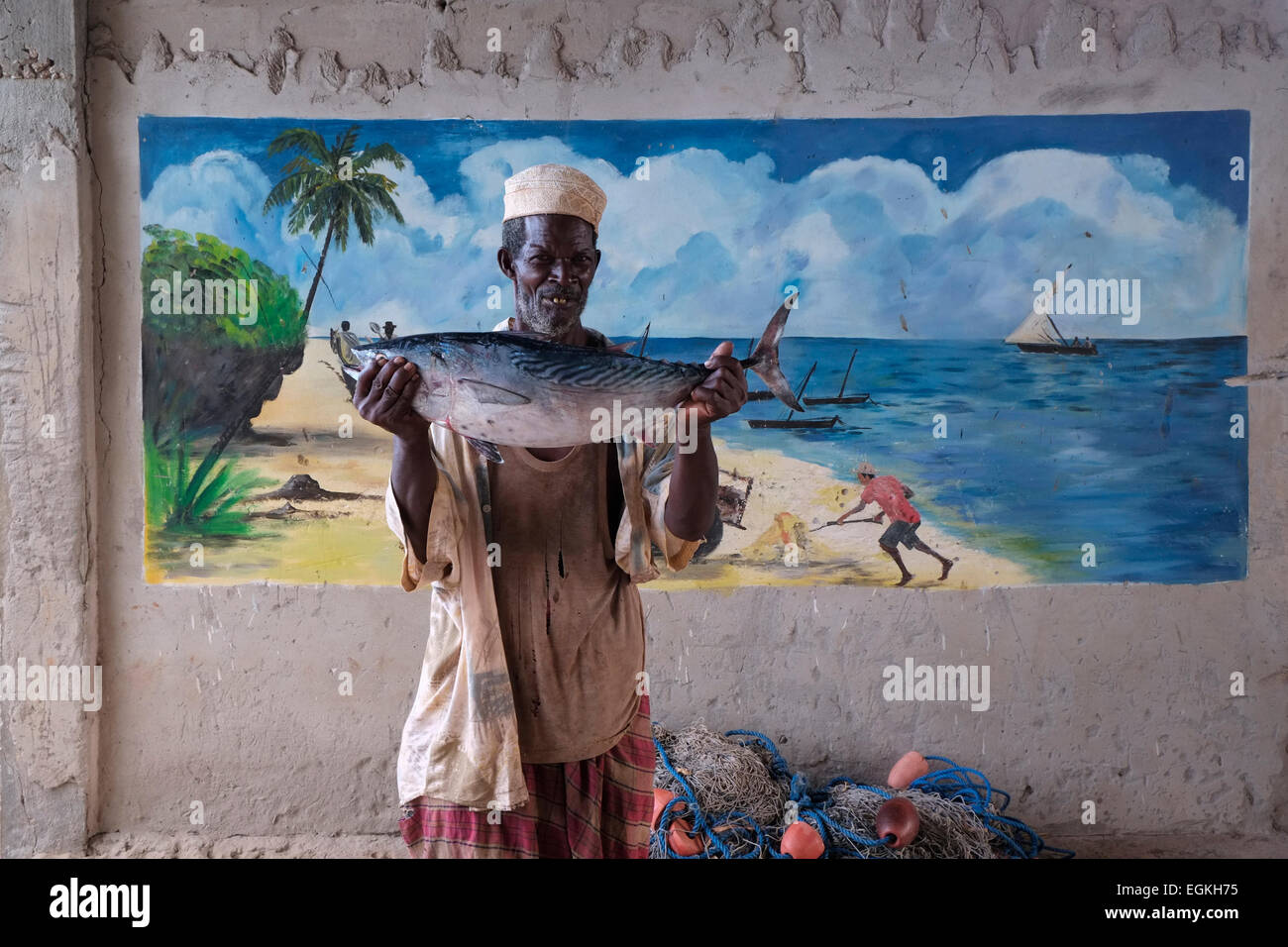 A fishmonger holds a Tuna fish as he stands next to a painted wall in ...