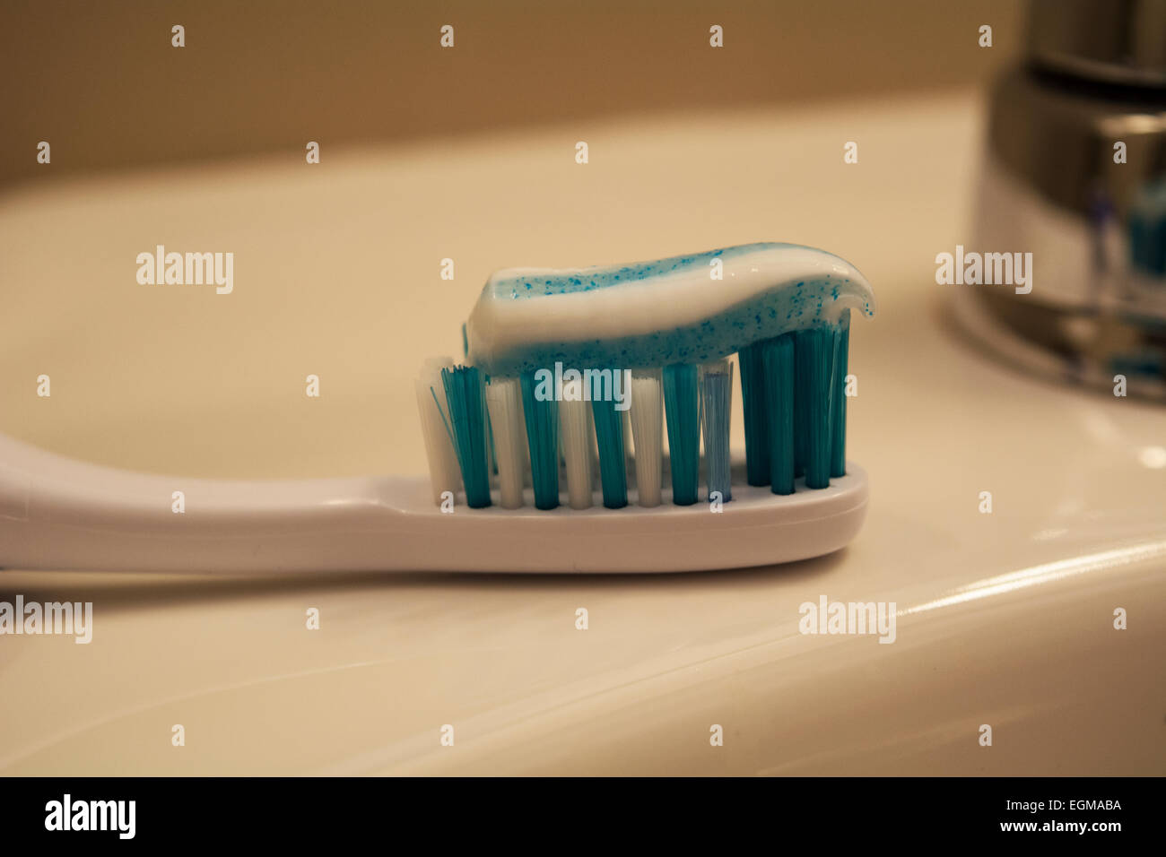 A toothbrush resting on a sink with a swirl of toothpaste of top of the ...