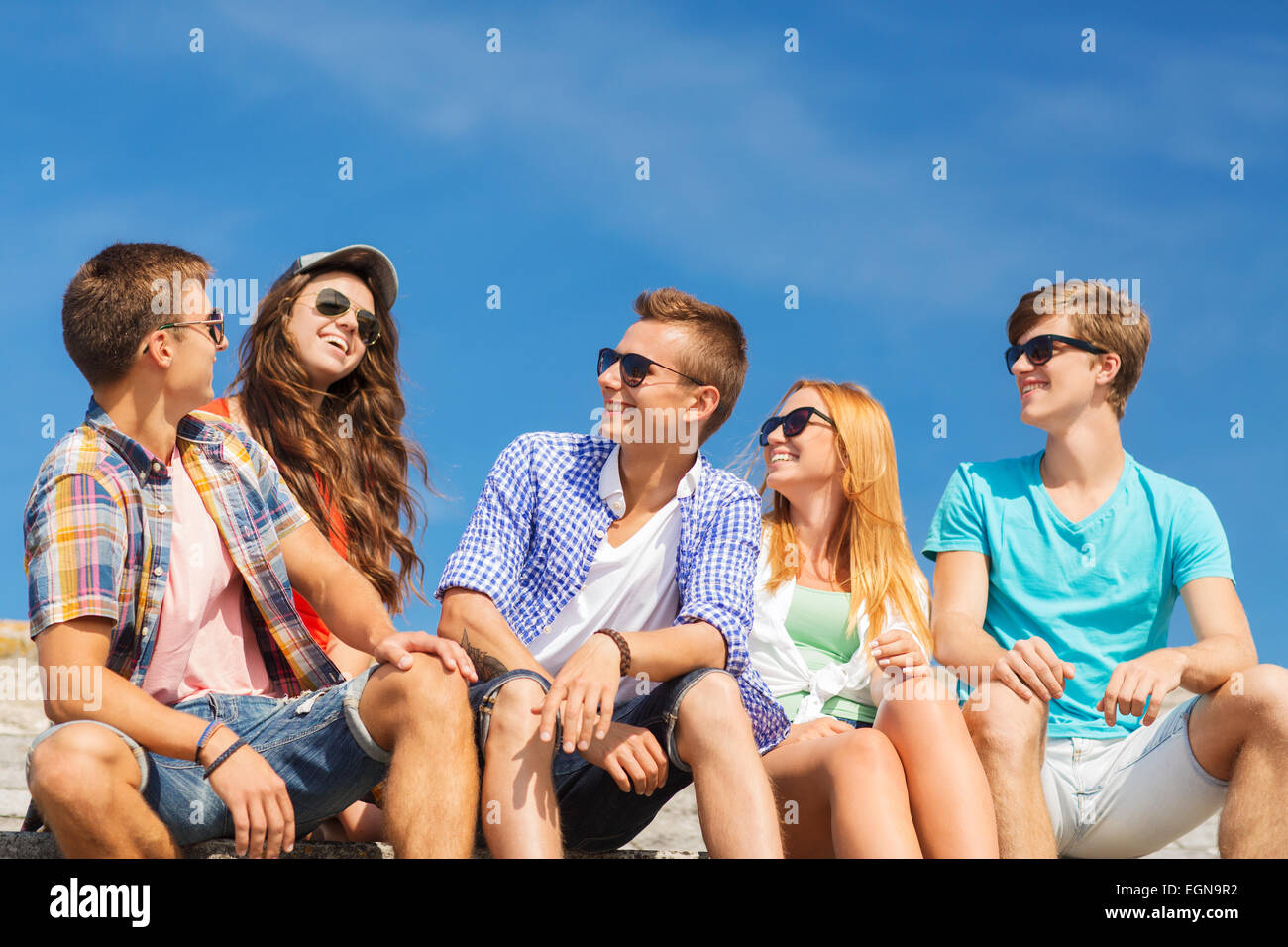 group of smiling friends sitting on city street Stock Photo - Alamy