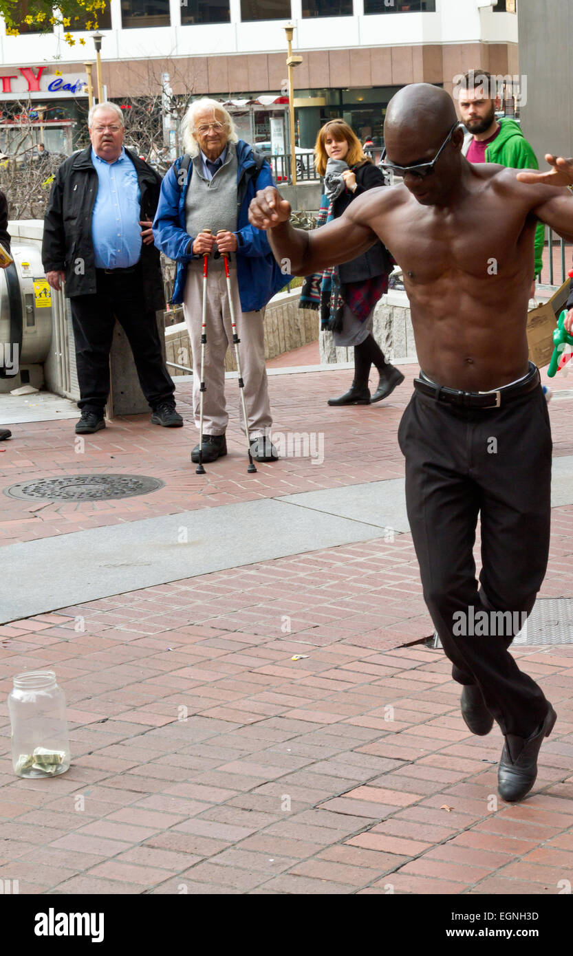An athletic, young black man street dancing with donation jar on ground ...