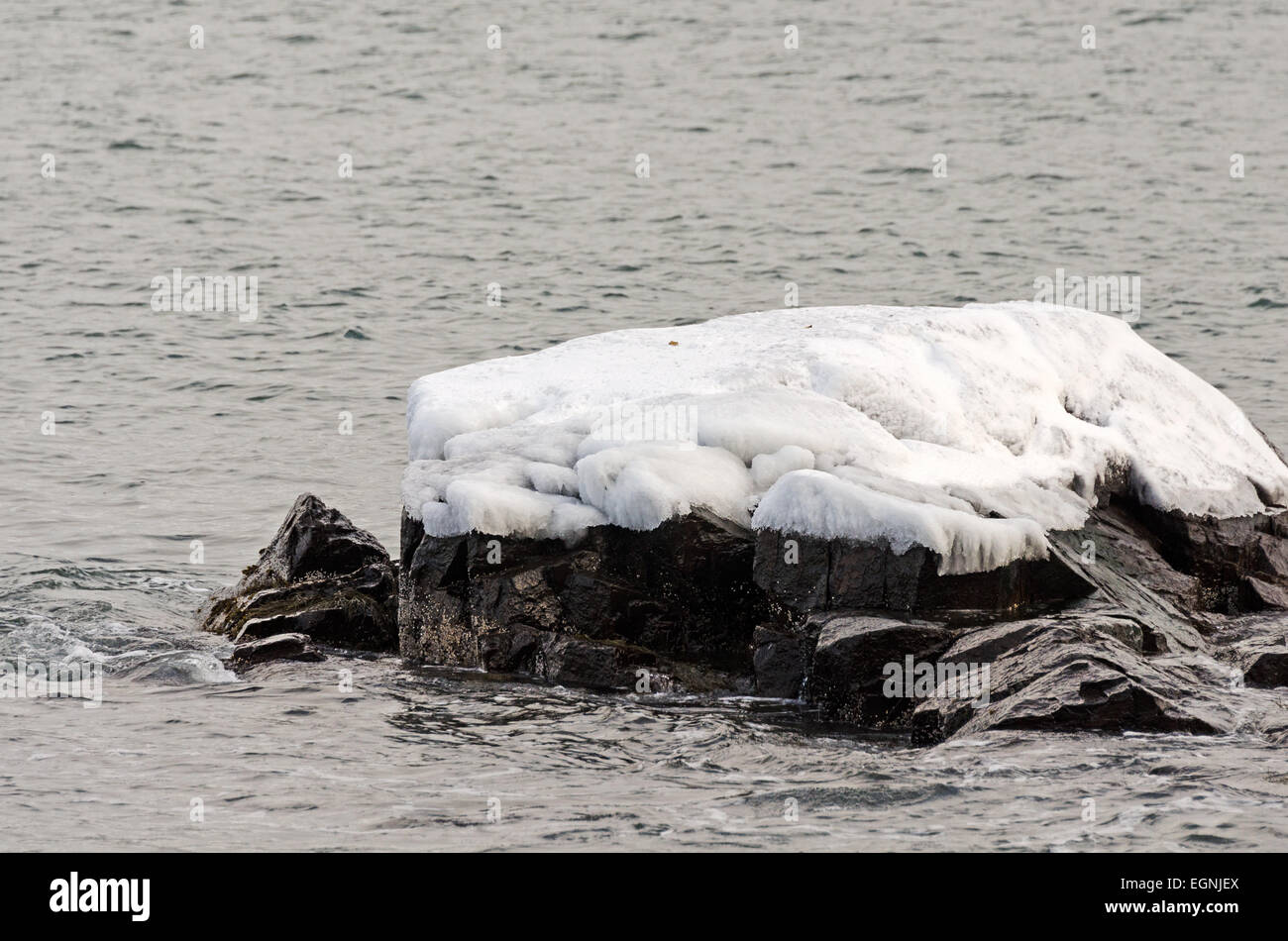 A thick crust of ice and snow tops a boulder on the coast of Maine ...